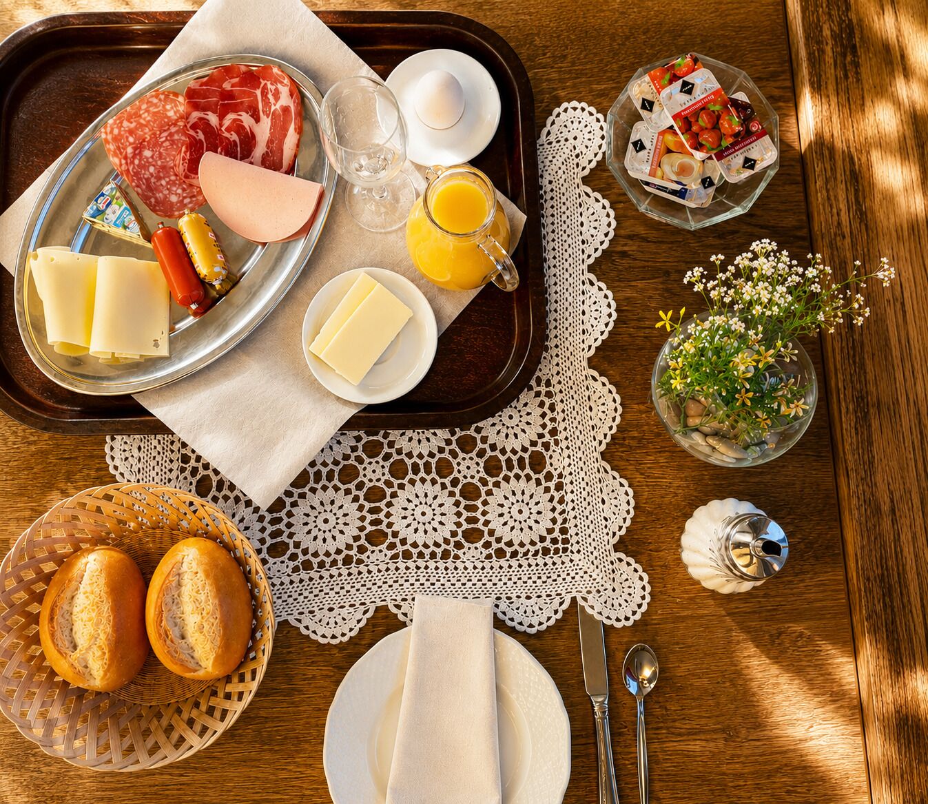Uma bandeja de café da manhã com diversos alimentos, um copo de suco de laranja e um sobrefolho decorativo sobre uma mesa de madeira.