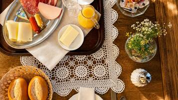 Uma bandeja de café da manhã com diversos alimentos, um copo de suco de laranja e um sobrefolho decorativo sobre uma mesa de madeira.