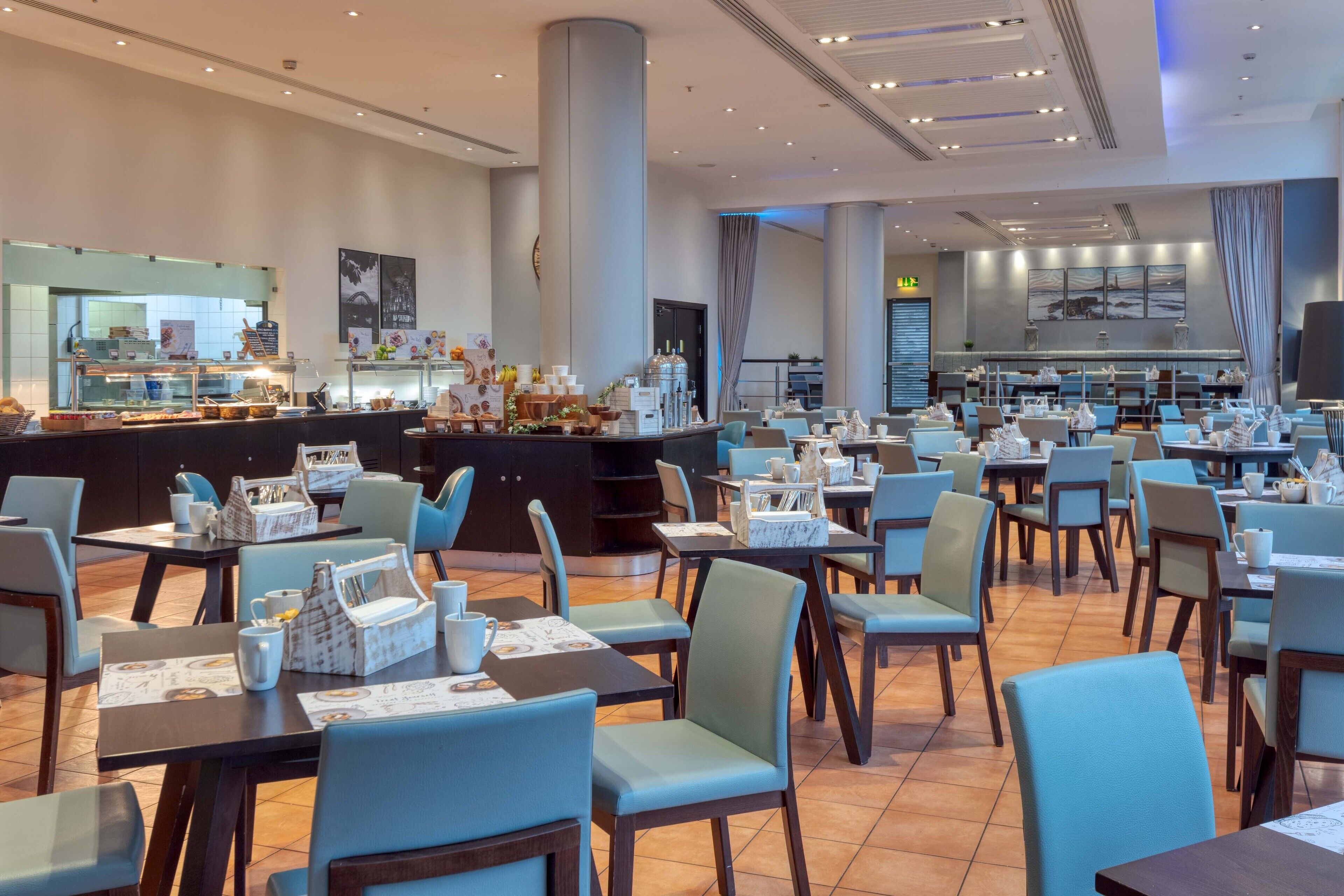 Ampla área de jantar de hotel, com várias mesas e cadeiras, um buffet e design de interiores moderno.