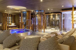 Uma área de spa moderna com hidromassagem, assentos com almofadas estampadas e um espaço de chuveiro com divisória de vidro.