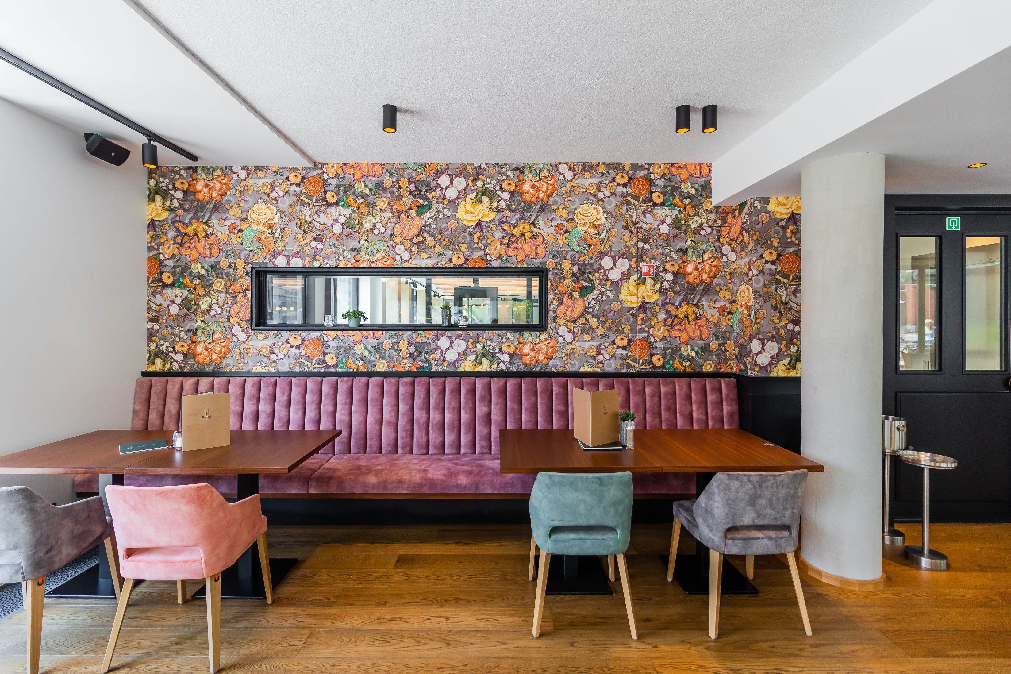Um restaurante com um mural floral na parede, mesa de madeira e assentos acolchoados.