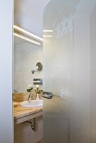 Casa de banho com lavatório, espelho e porta de vidro jateado.