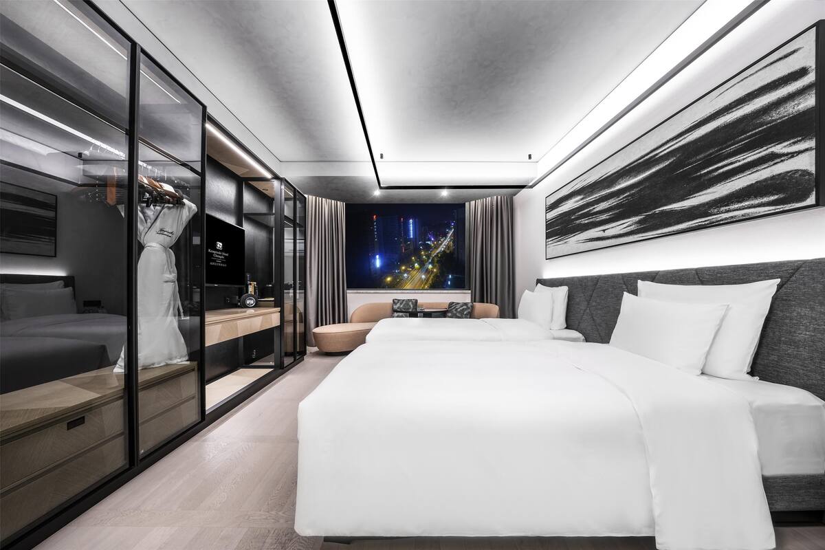 Quarto moderno com uma cama grande, guarda-roupa com portas de vidro e vista para a cidade pela janela.