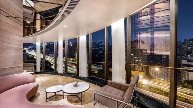 Interior moderno com teto curvo, grandes janelas e vista noturna da cidade.