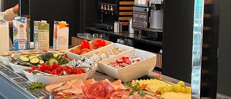 Buffet com diversos itens de comida, incluindo carnes, queijos, frutas e legumes.