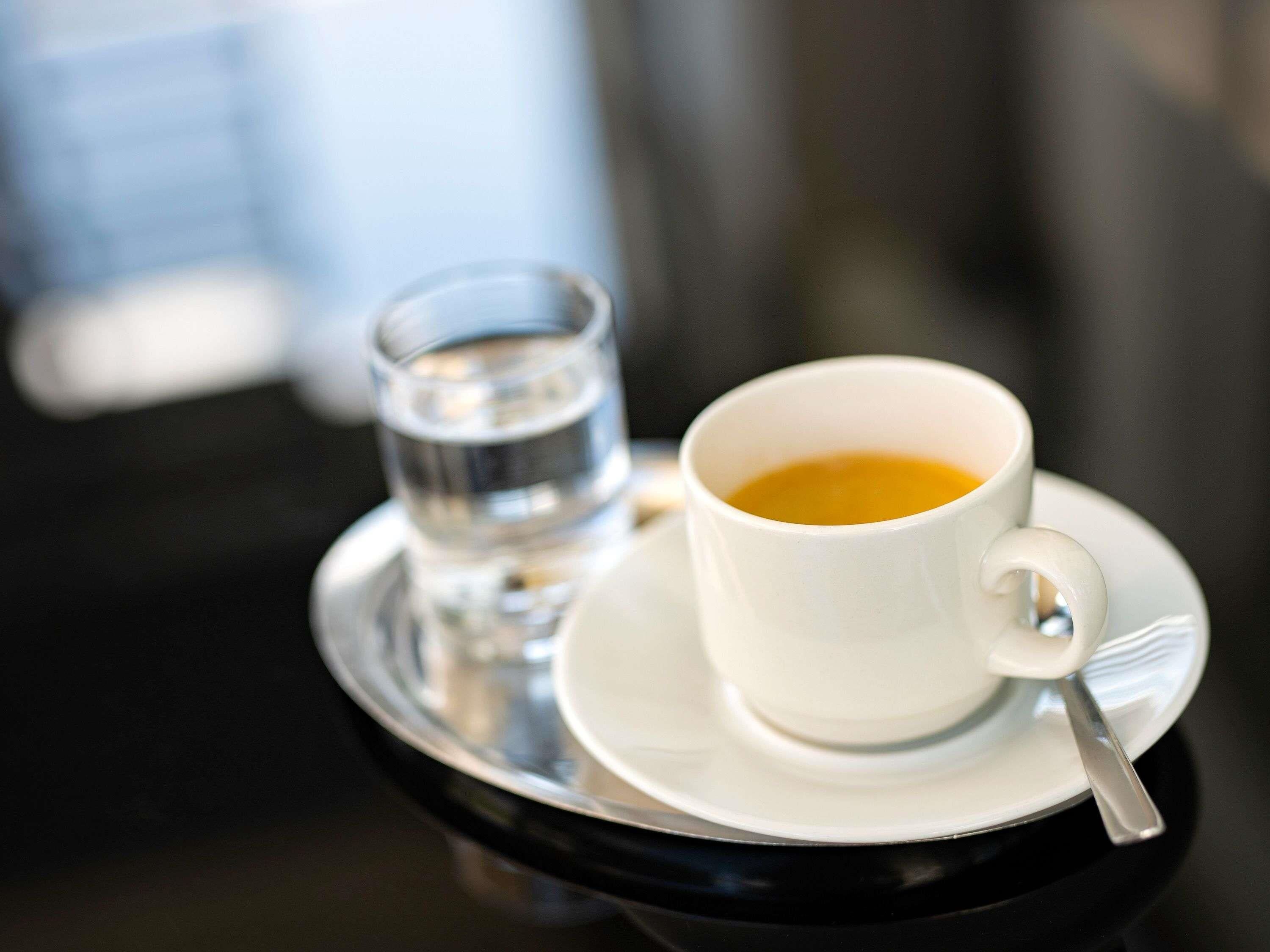 Uma chávena de café branco num pires, com uma colher, acompanhada por um copo de água num tabuleiro.