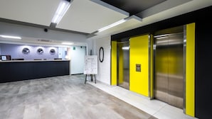 Uma área de recepção moderna com balcão, relógios e elevador.