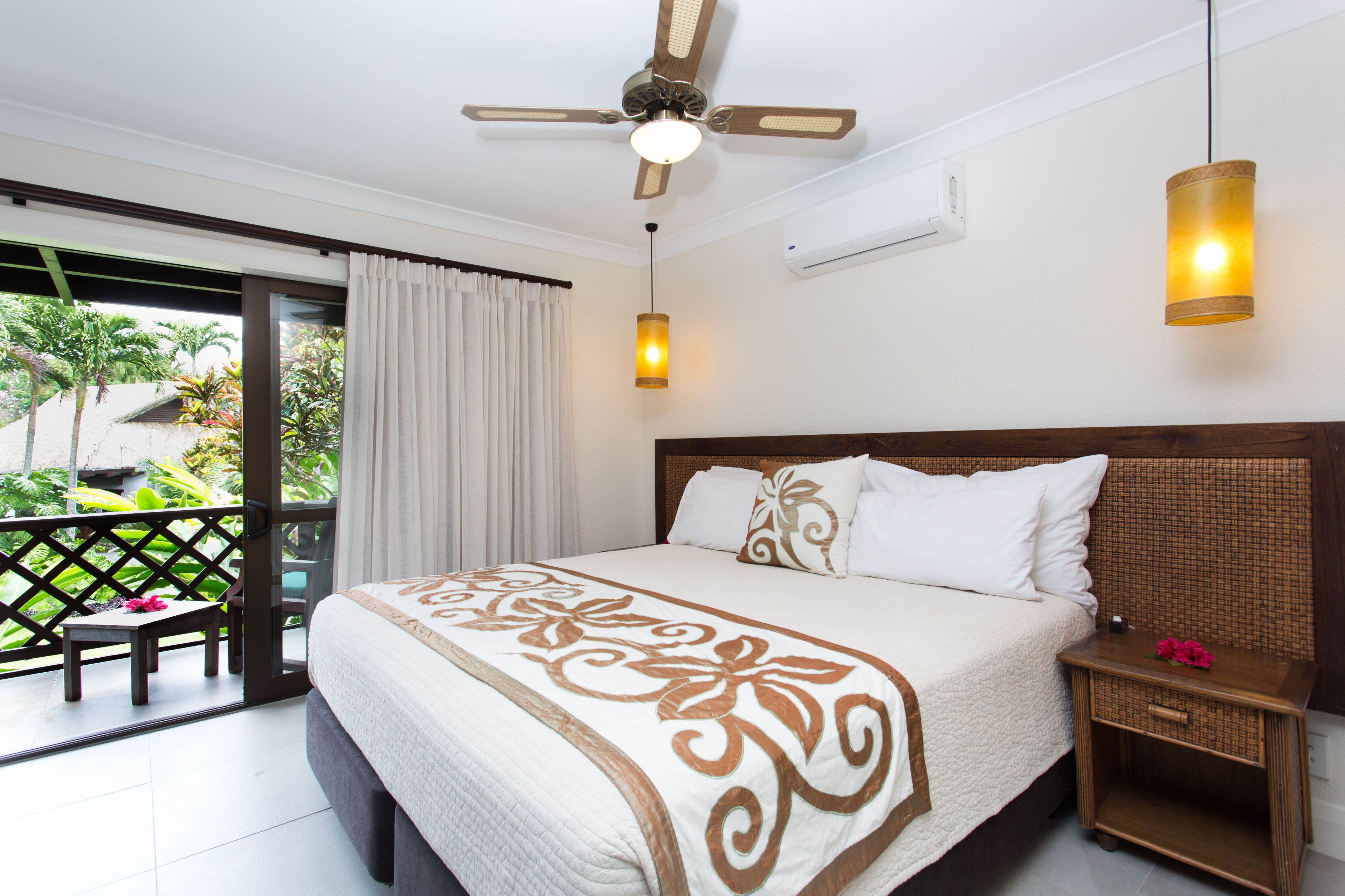 Quarto de hotel com cama, ventoinha no teto, mesa de cabeceira e vista para o exterior.