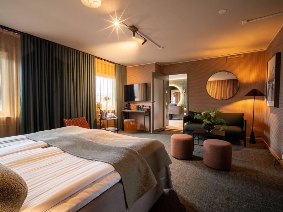 Quarto de hotel moderno com uma cama grande, uma escrivaninha, um sofá e um espelho redondo.