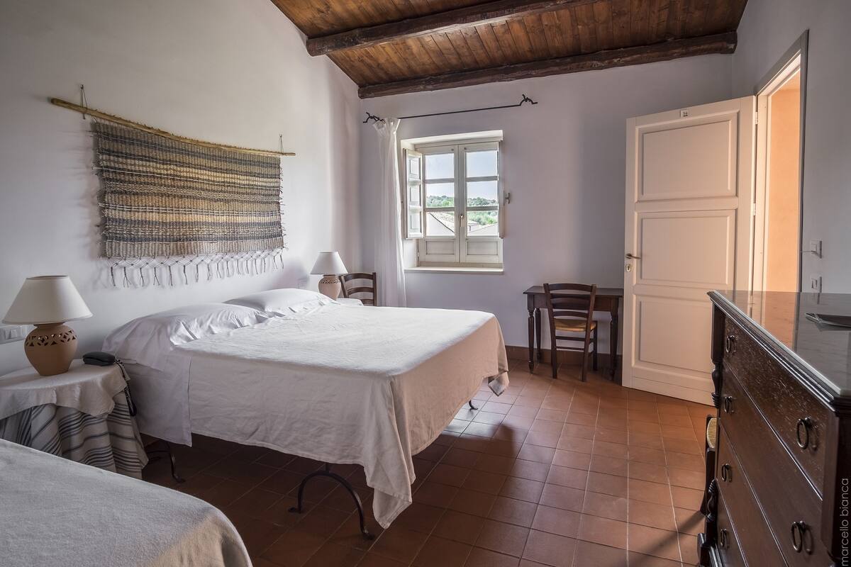 Quarto com cama, mesas de cabeceira, luminária, cadeira, guarda-roupa e janela com vista.