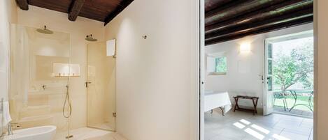 Casa de banho moderna com chuveiro de vidro, sanita e lavatório. Uma porta dá para uma varanda com mesa e cadeiras.
