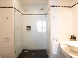 Uma casa de banho moderna com chuveiro envidraçado, lavatório branco e um porta-toalhas.