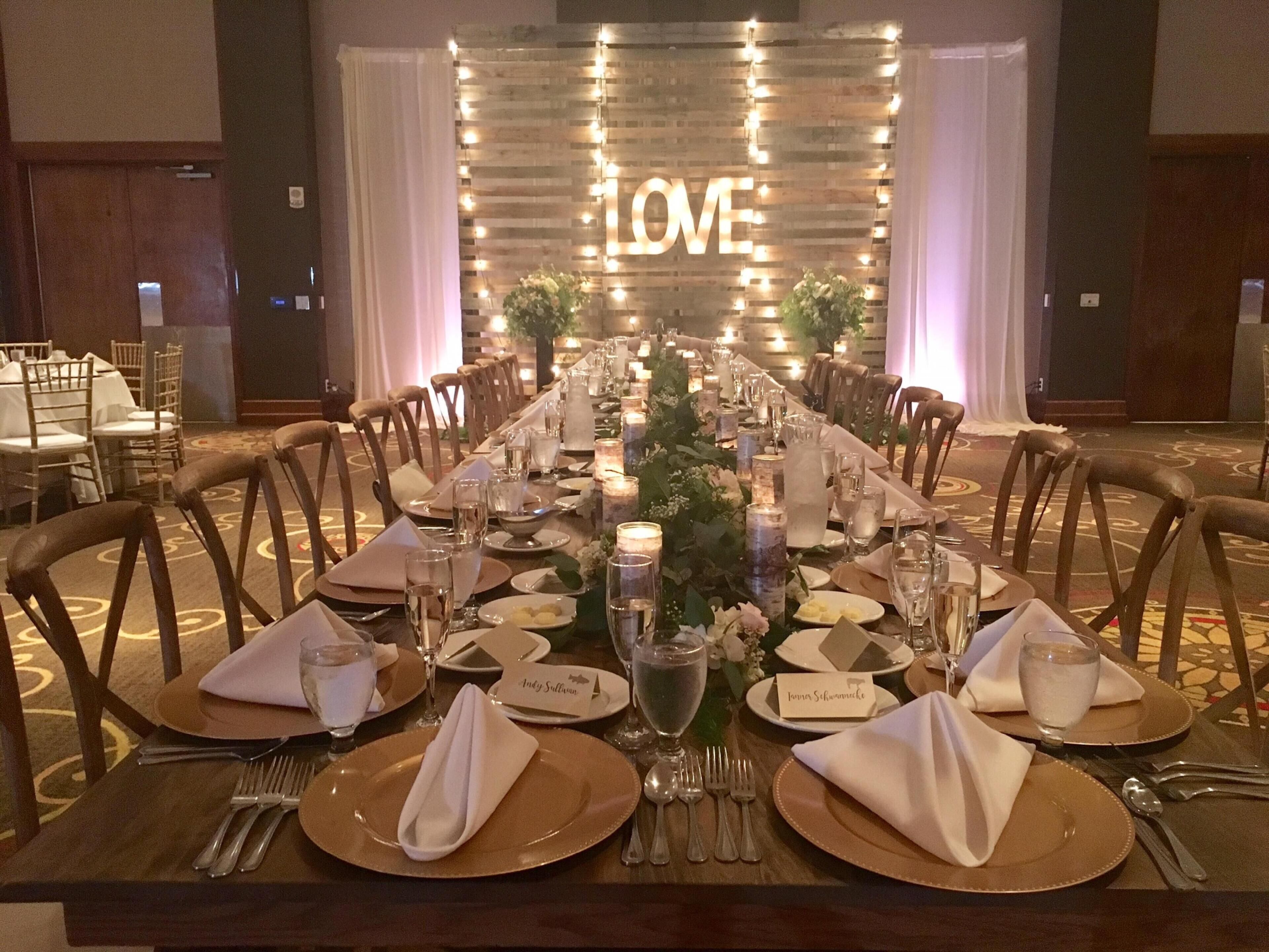 Uma longa mesa de jantar posta para um evento formal, com cartões de lugar, velas e arranjos florais.