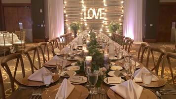 Uma longa mesa de jantar posta para um evento formal, com cartões de lugar, velas e arranjos florais.