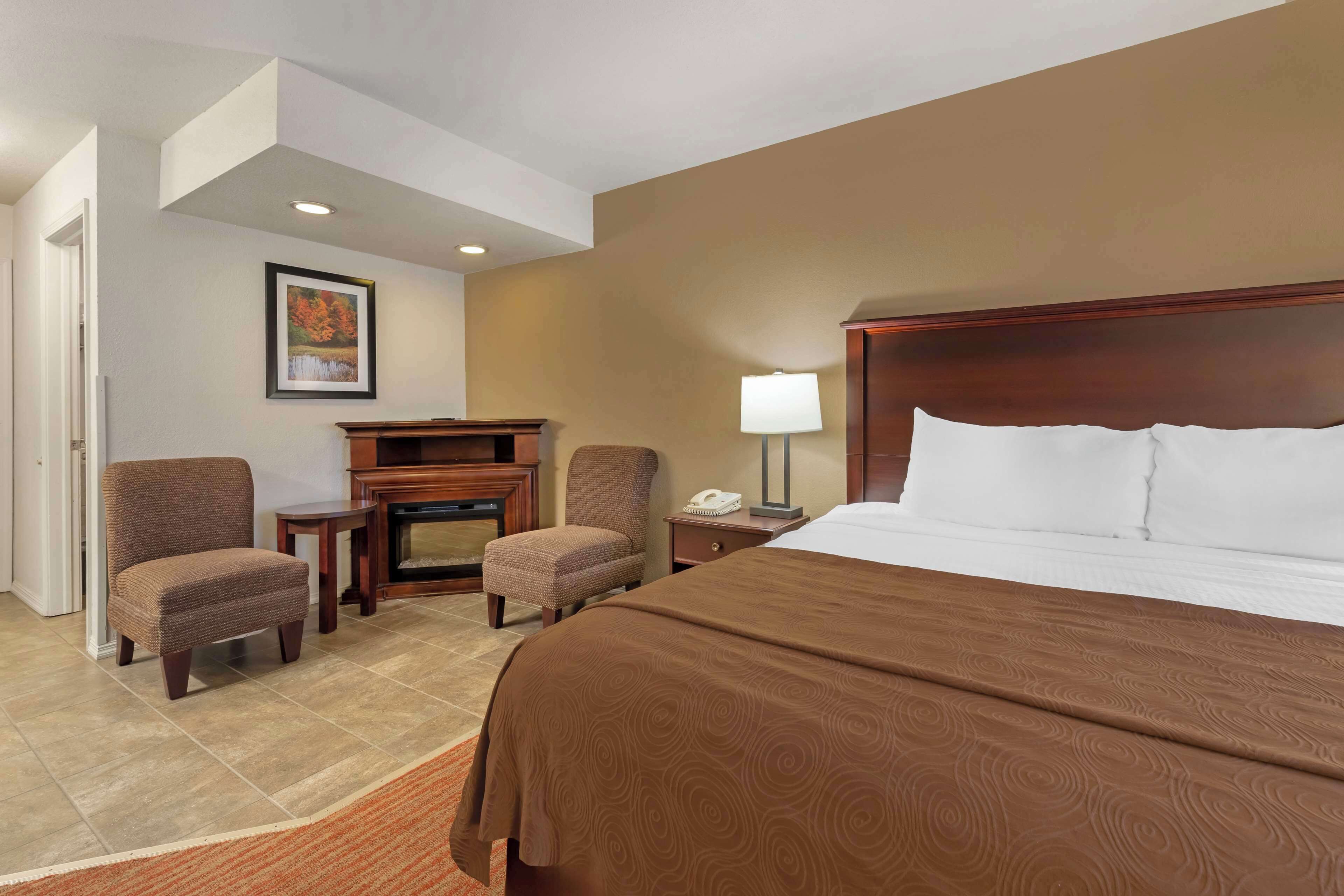 Quarto de hotel com uma cama grande, duas poltronas, uma mesinha, um abajur e uma lareira.