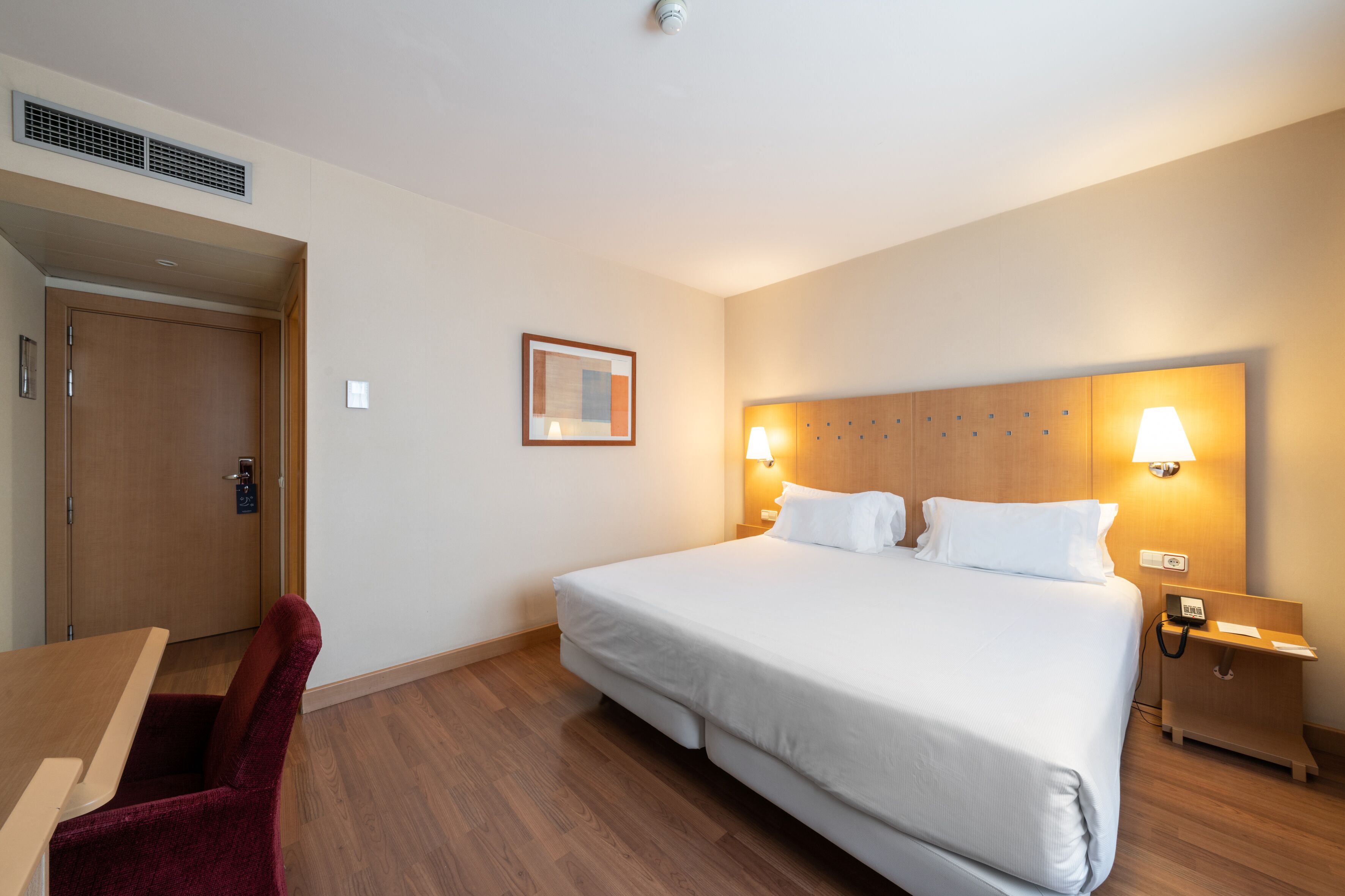 Quarto de hotel com cama grande, abajures, escrivaninha e uma cadeira.