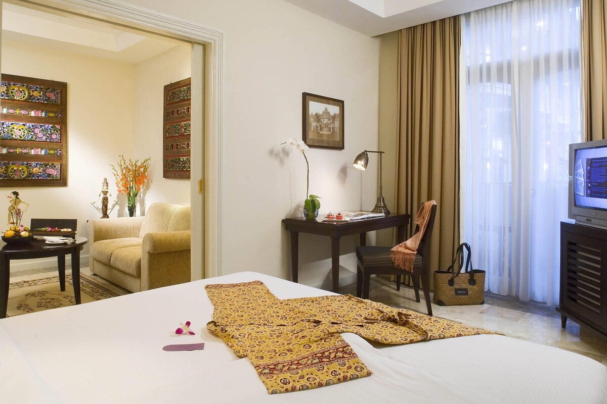 Quarto de hotel com cama, escrivaninha, cadeira, televisão e janela com cortinas.