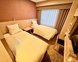 Quarto de hotel com duas camas, uma mesinha de cabeceira, televisão e janela com cortinas.