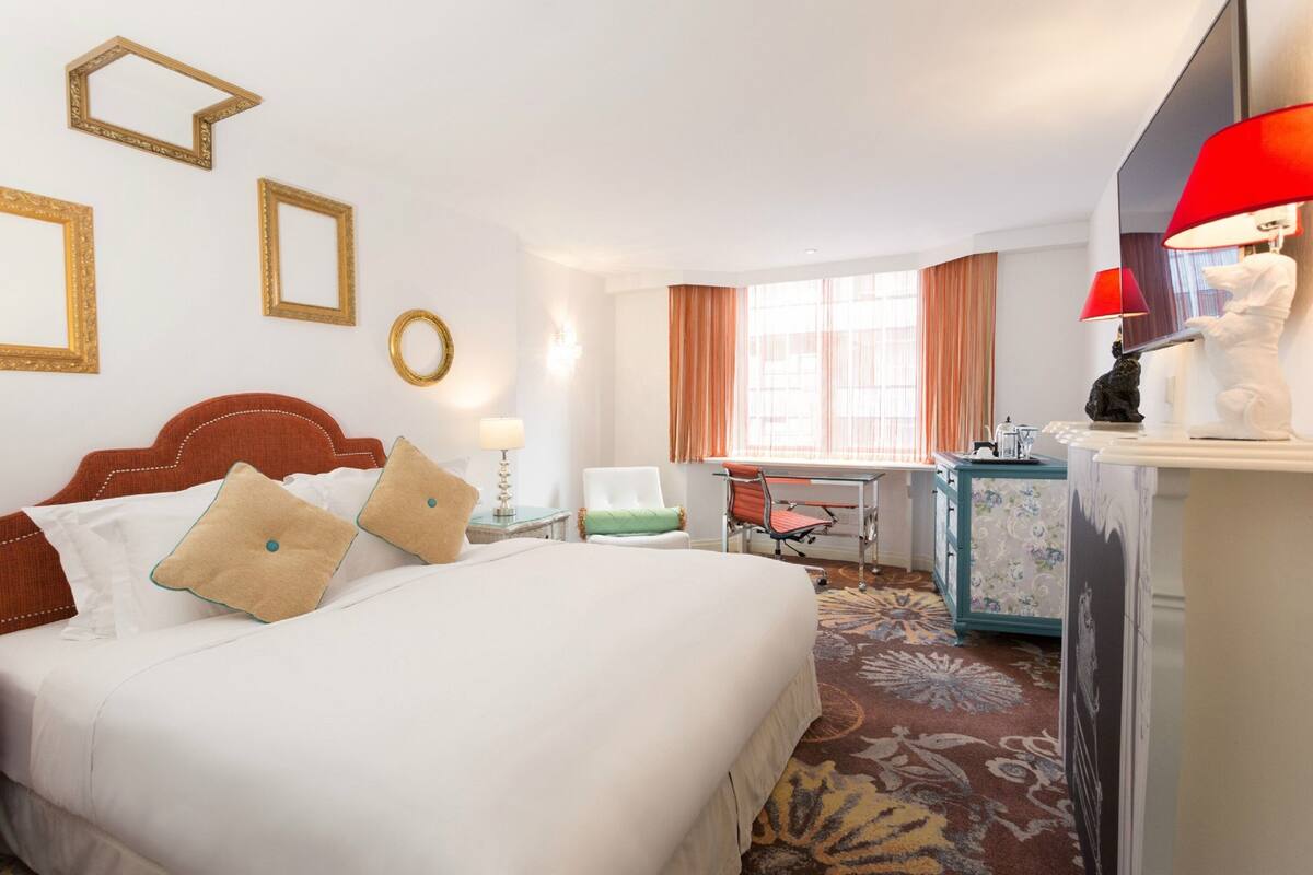 Quarto de hotel com cama, escrivaninha, cadeira, cômoda e espelho.