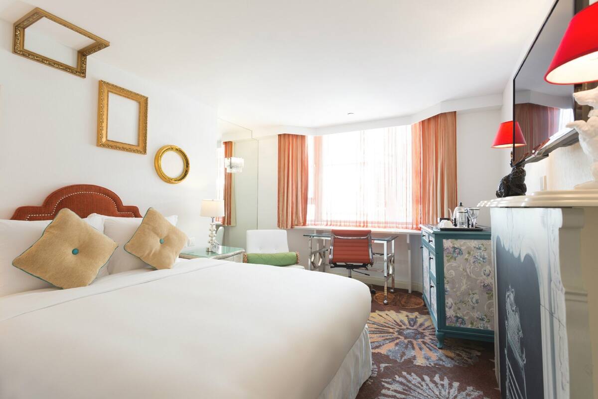 Quarto de hotel com uma cama grande, uma escrivaninha, uma cadeira e um armário.