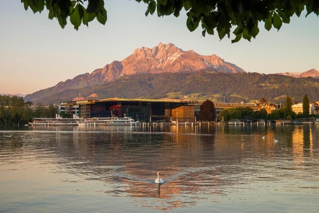 Um rio com um cisne, um barco e um edifício com uma montanha ao fundo.