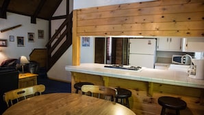 Cozinha acolhedora com detalhes em madeira, área de jantar com mesa redonda e cadeiras, e uma geladeira visível.