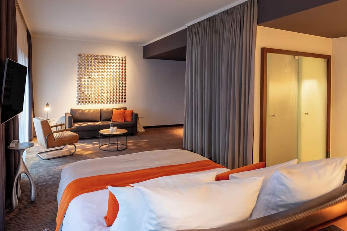 Quarto de hotel com duas camas, um sofá, uma mesa de centro, uma televisão e uma luminária fixada na parede.