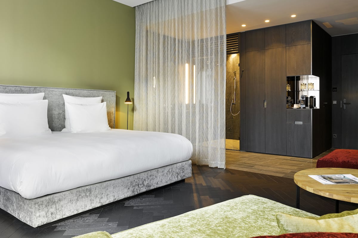 Quarto de hotel moderno com uma cama grande, guarda-roupa, escrivaninha e área de chuveiro.