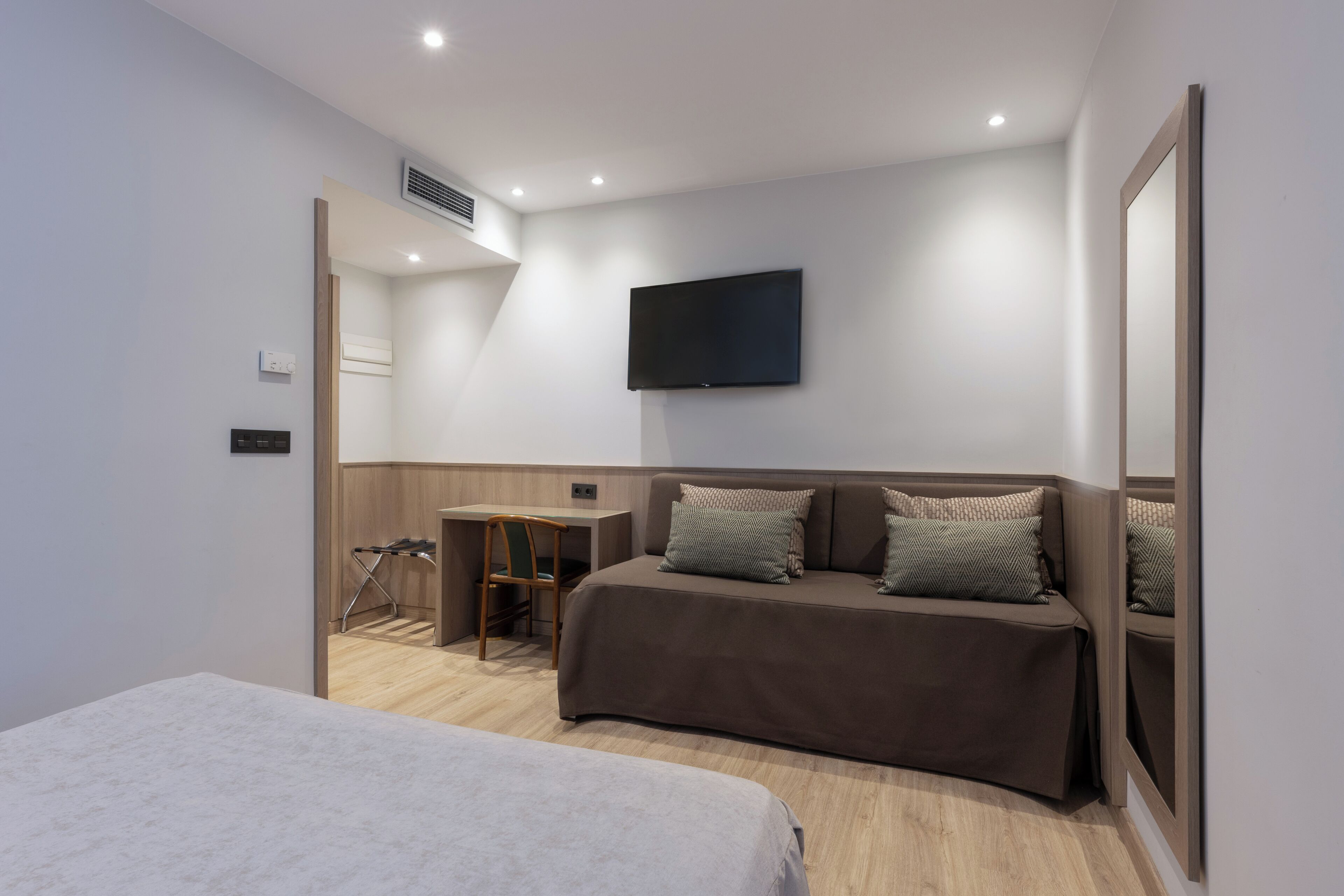 Quarto de hotel moderno com uma cama, uma escrivaninha, uma cadeira e uma TV de tela plana fixada na parede.
