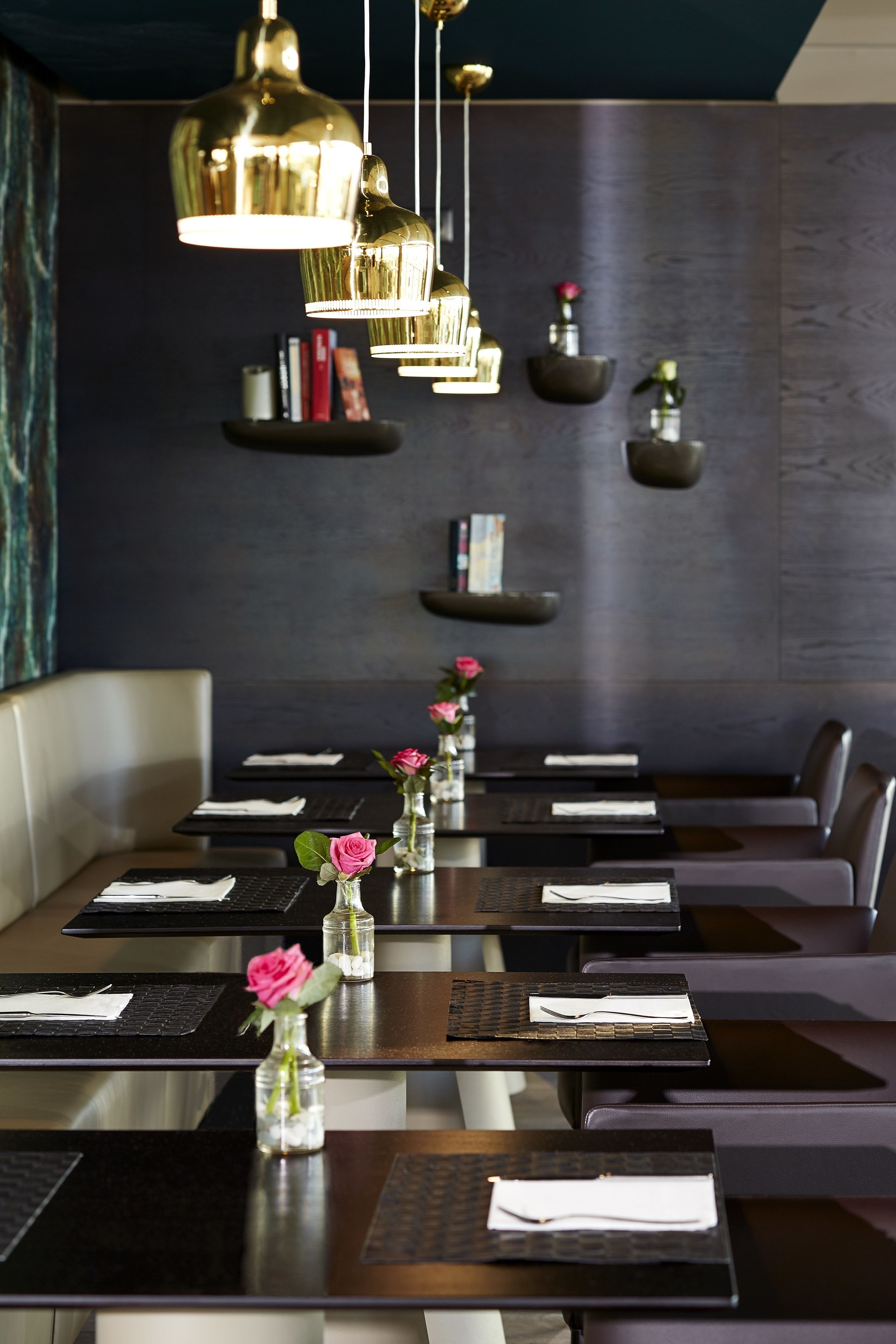 Um restaurante com uma mesa de jantar comprida, jogos americanos pretos e pequenos vasos com flores cor-de-rosa.