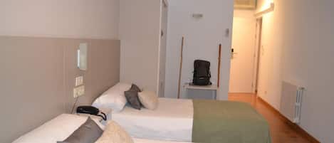 Quarto de hotel com duas camas, telefone de apoio, radiador e porta que dá para outro aposento.