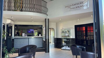 Um saguão de hotel com balcão de recepção, área de estar e uma vitrine de vidro com garrafas.