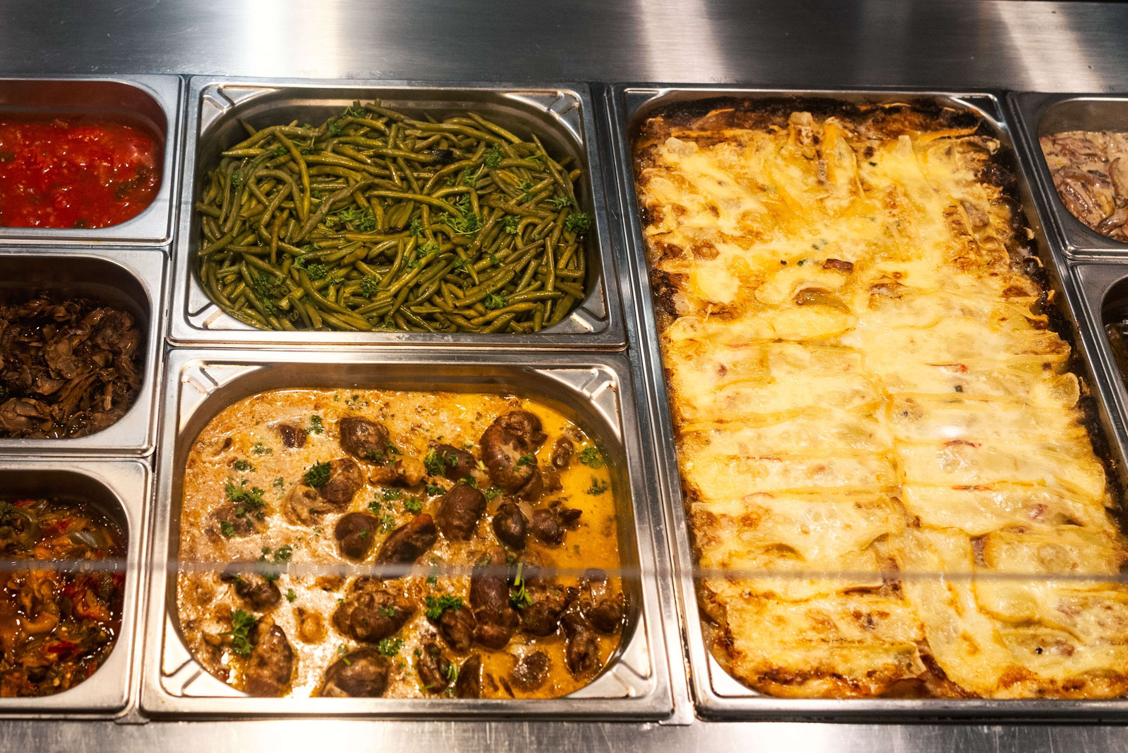 Buffet com diversos pratos, incluindo vagem, um prato de carne e um ensopado assado.