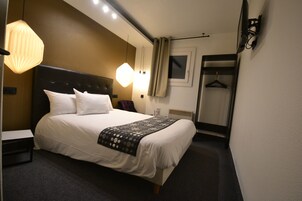 Quarto de hotel com cama, mesa de cabeceira, abajur e espelho.