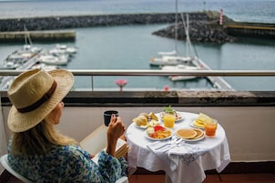 Uma pessoa sentada à mesa com uma refeição, com vista para um porto cheio de barcos.