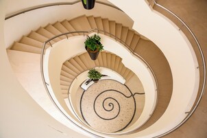 Escadaria em espiral com degraus bege e piso em mosaico circular.