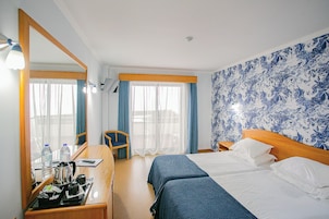 Quarto de hotel com cama, escrivaninha, cadeira, espelho e parede com padrão azul.
