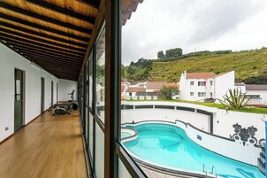 Vista de uma piscina a partir de uma varanda coberta, com equipamento de ginástica visível.