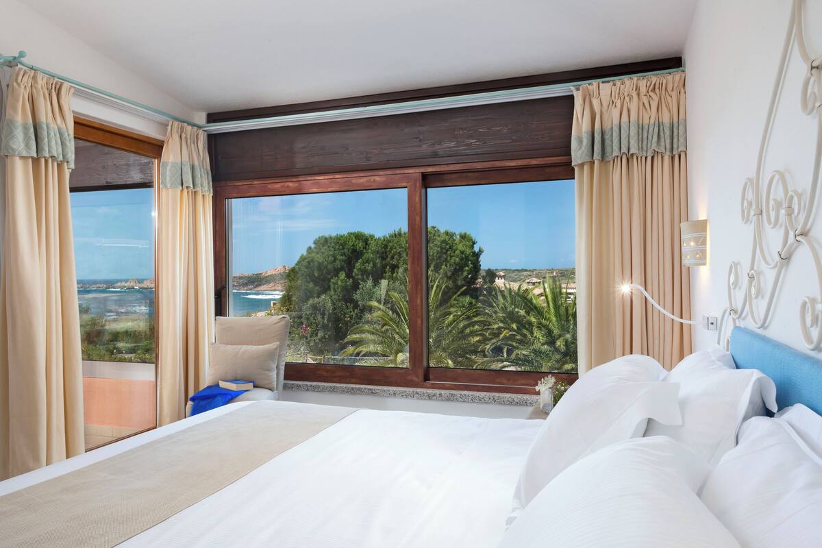 Quarto com cama grande, vista para o mar e varanda com cortinas.