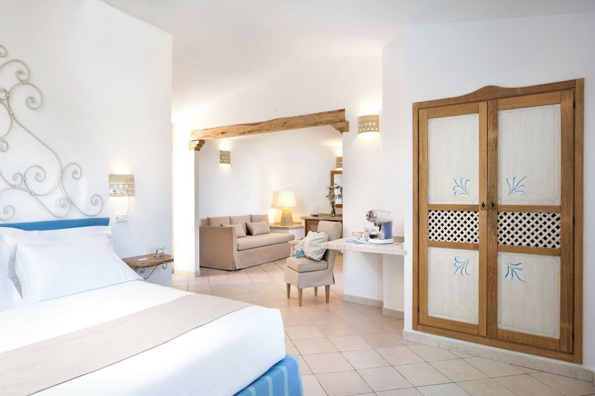 Quarto de hotel com cama, escrivaninha, sofá e guarda-roupa.