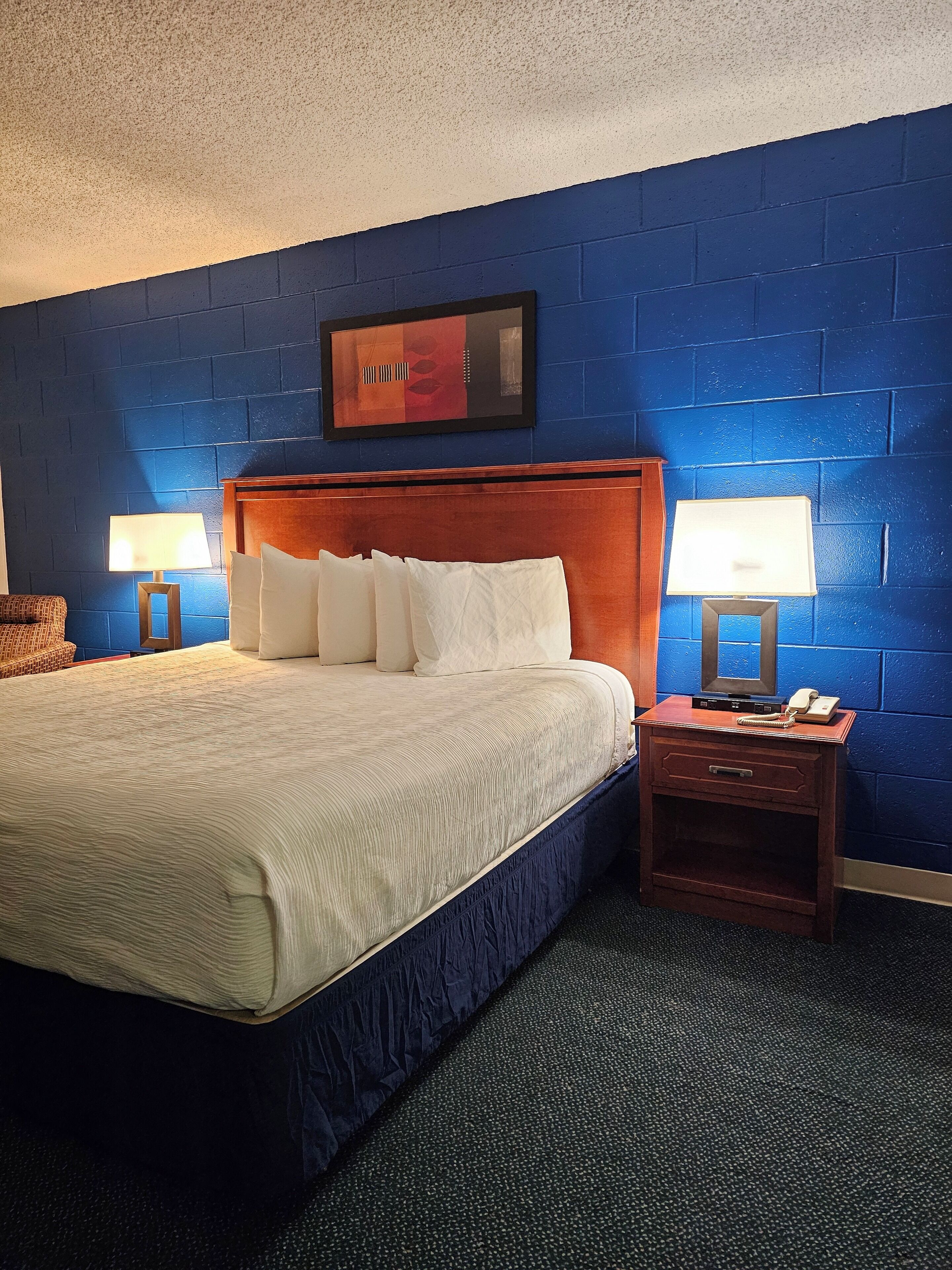 Quarto de hotel com uma cama grande, duas mesas de cabeceira com abajures, uma cabeceira de madeira e uma parede de tijolos azuis.