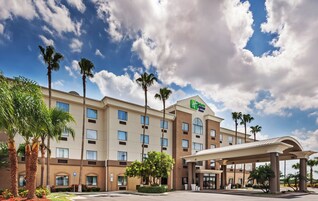 Um hotel Holiday Inn Express com entrada coberta, palmeiras e céu claro.