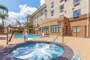 Área de piscina de hotel com hidromassagem, espreguiçadeiras e um edifício com várias janelas.
