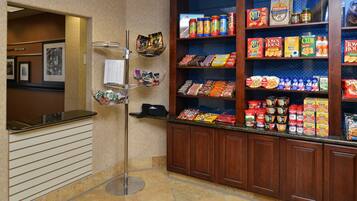 Um saguão de hotel com balcão de recepção, bar de petiscos e diversas opções de comida e bebida.