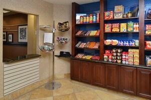 Um saguão de hotel com balcão de recepção, bar de petiscos e diversas opções de comida e bebida.