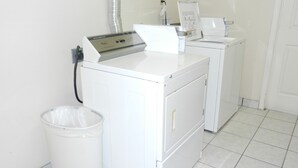 Uma lavanderia com máquina de lavar frontal, secadora e lixeira.