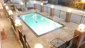 Uma piscina exterior com um deck ladrilhado, rodeada por um portão baixo e iluminada por esferas luminosas.
