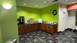 Uma cozinha com paredes verdes, armários de madeira, piso de azulejos estampados e um relógio na parede.