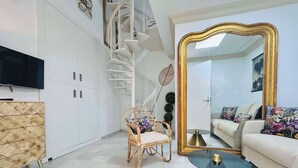 Uma sala de estar moderna com escada em espiral, um espelho grande, um sofá com almofadas florais e uma mesa de centro de vidro.