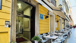 Fachada de hotel com área de estar externa, tapete vermelho na entrada e placa azul indicando acesso para pessoas com deficiência.